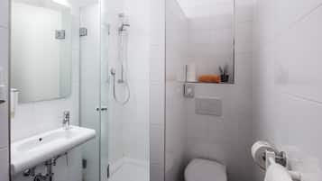 Uma casa de banho moderna com chuveiro de vidro, lavatório branco e sanita.