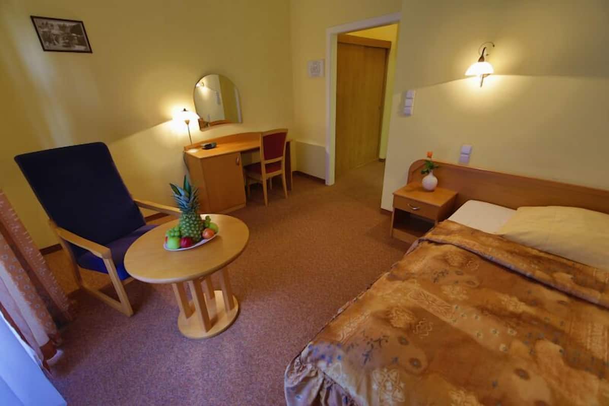 Quarto de hotel com uma cama, uma escrivaninha com cadeira, uma mesinha com frutas e uma mesinha de cabeceira com abajur.