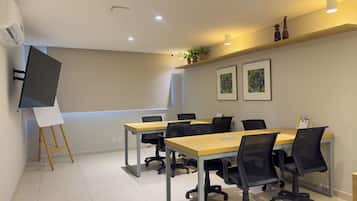 Sala de conferência com uma mesa grande, cadeiras, projetor e obras de arte na parede.