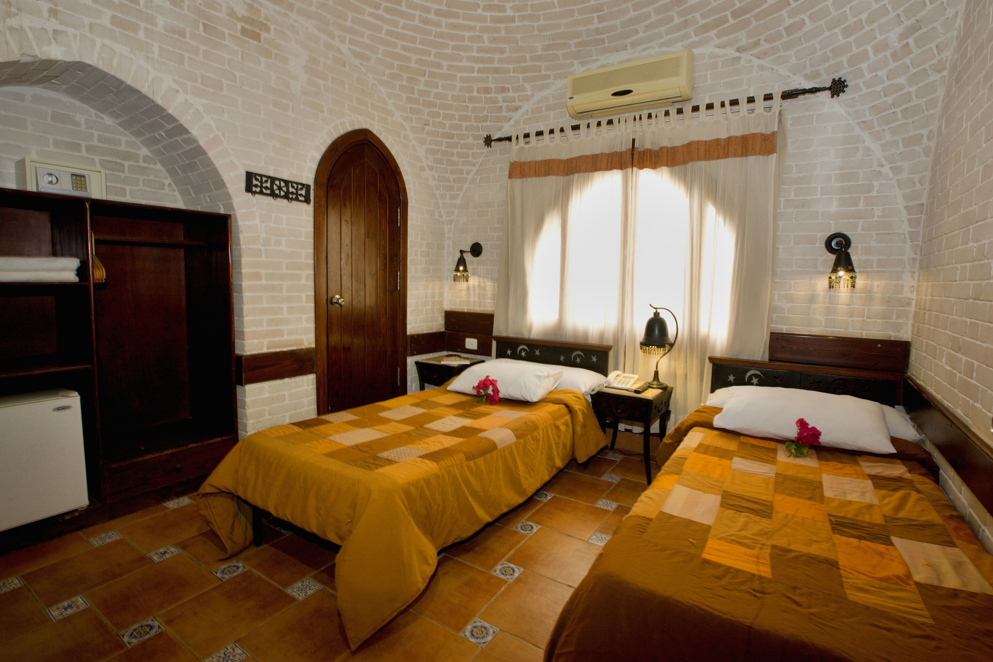 Quarto com duas camas, um guarda-roupa, um aquecedor e uma janela com cortinas.