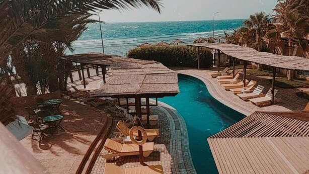 Uma área de piscina em resort, com piscina em formato de curva, espreguiçadeiras e guarda-sóis.