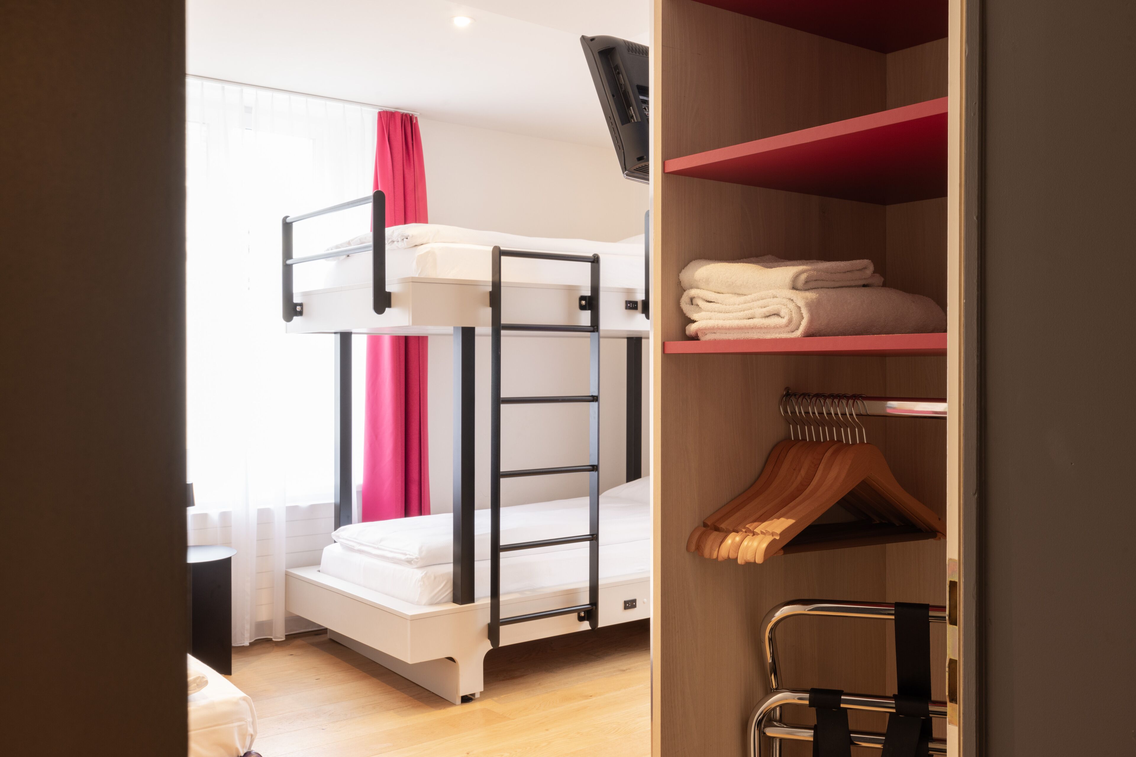 Quarto com beliches, guarda-roupa de madeira e escrivaninha.