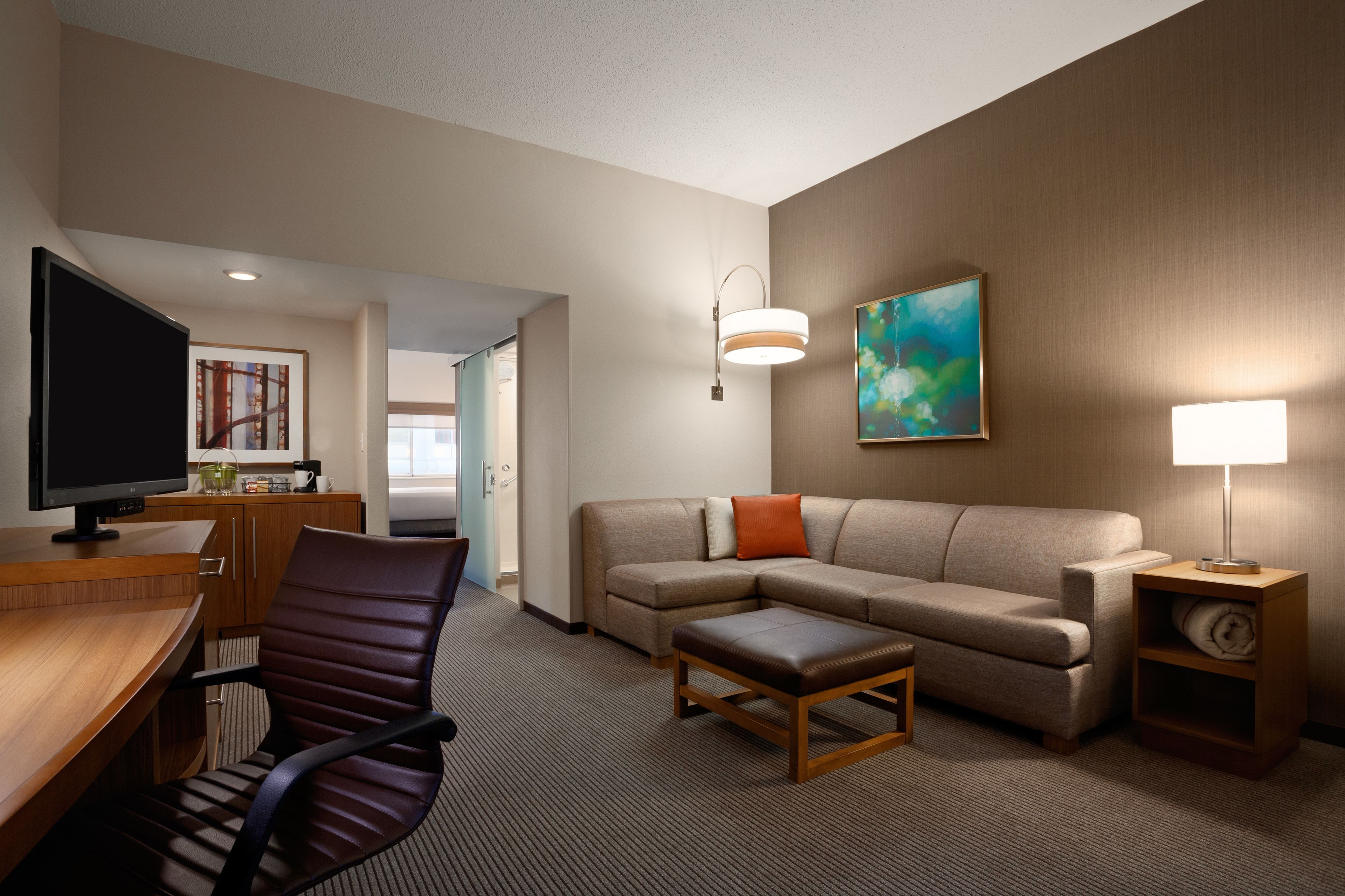 Quarto de hotel com sofá, mesa de centro, televisão, escrivaninha e luminária.