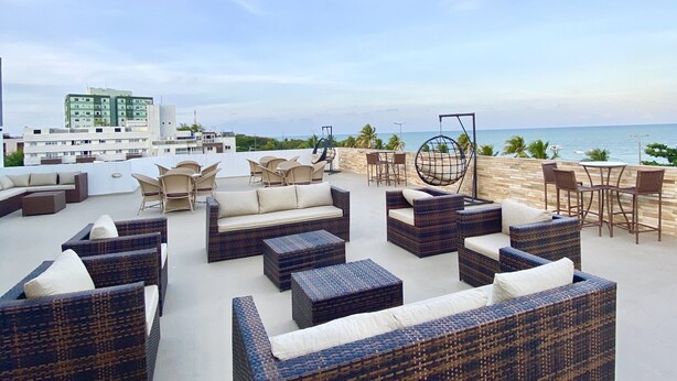 Um lounge no terraço com mobiliário de vime, piscina e vista para o oceano.