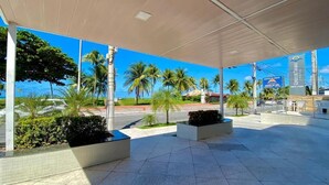 Uma área externa coberta com piso de azulejos, palmeiras e vista para o oceano.