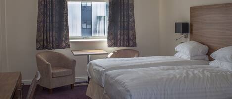 Quarto de hotel com duas camas, uma escrivaninha, uma cadeira e uma janela com cortinas.