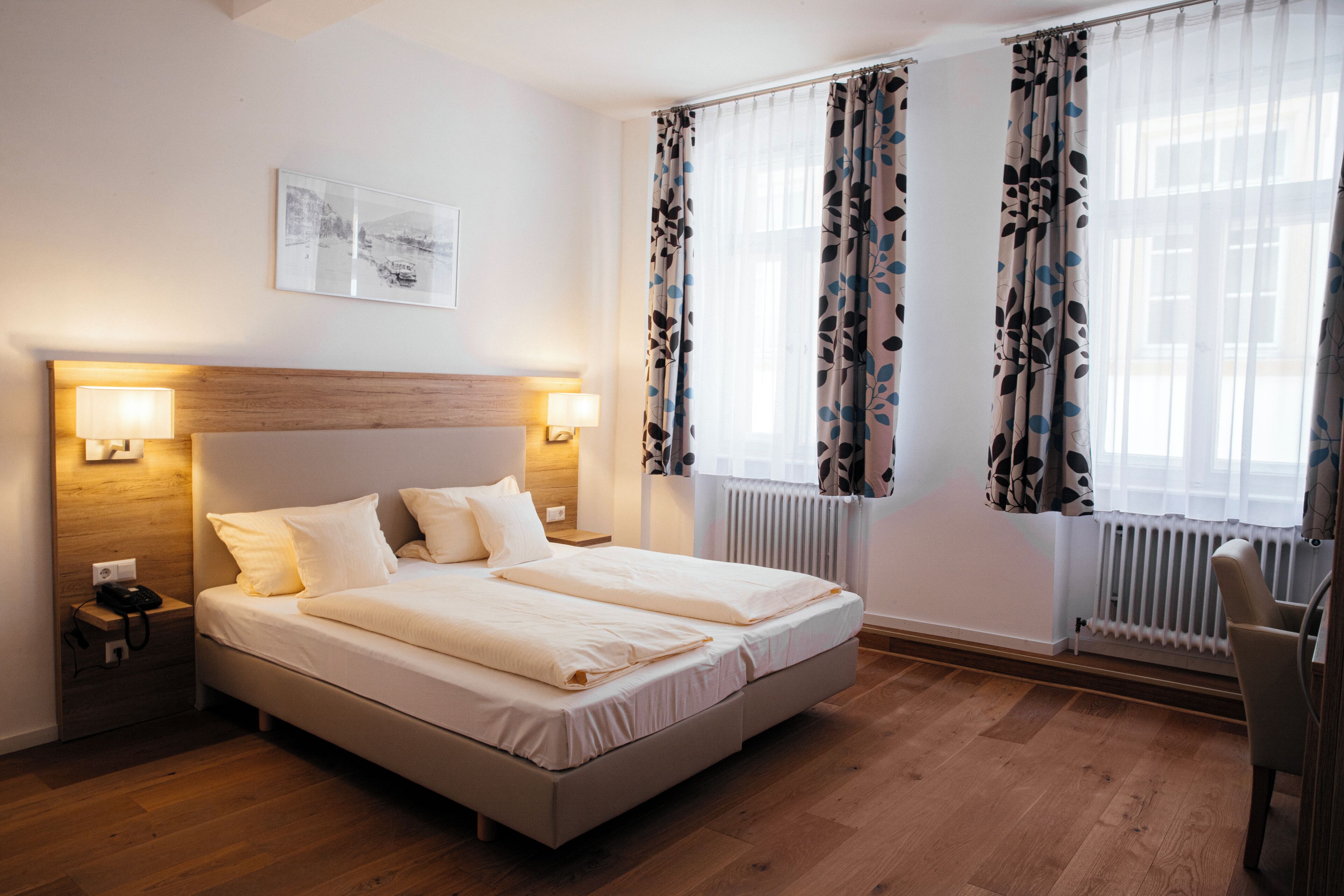 Uma cama de casal com cabeceira de madeira, luminárias de apoio e um quadro na parede.