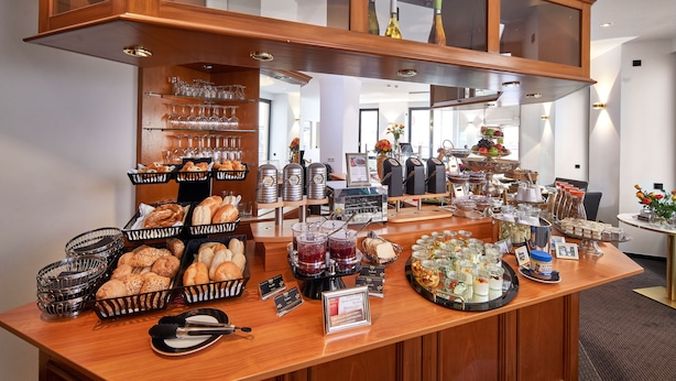 Balcão de buffet com diversos alimentos e bebidas, incluindo pão, doces e frutas.