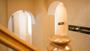 Corredor com placa indicando quartos 11 a 18, corrimão de madeira e uma porta com arco.