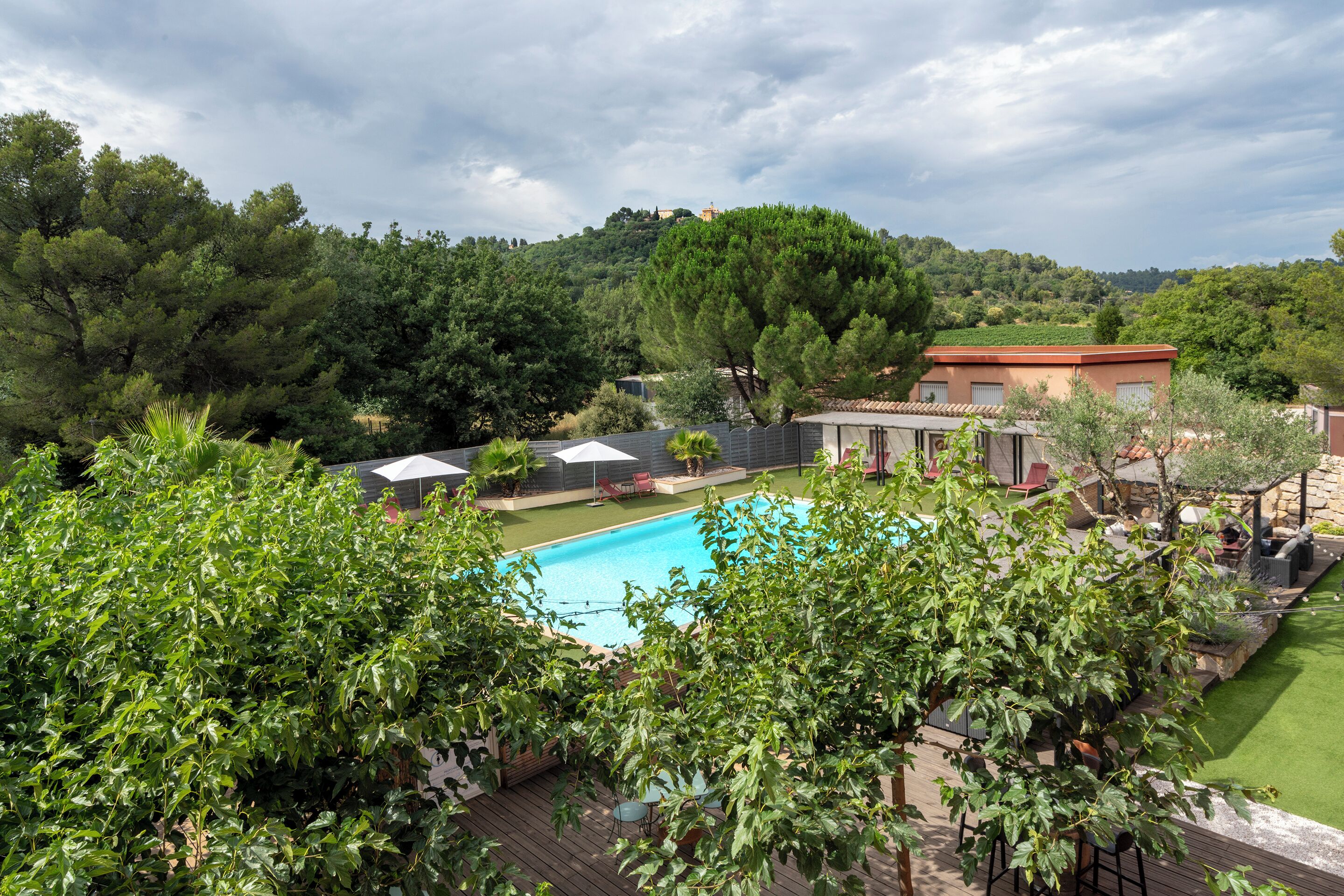 Uma piscina cercada por vegetação exuberante, uma área de pátio com mobiliário de exterior e vista para um morro com árvores e um edifício.