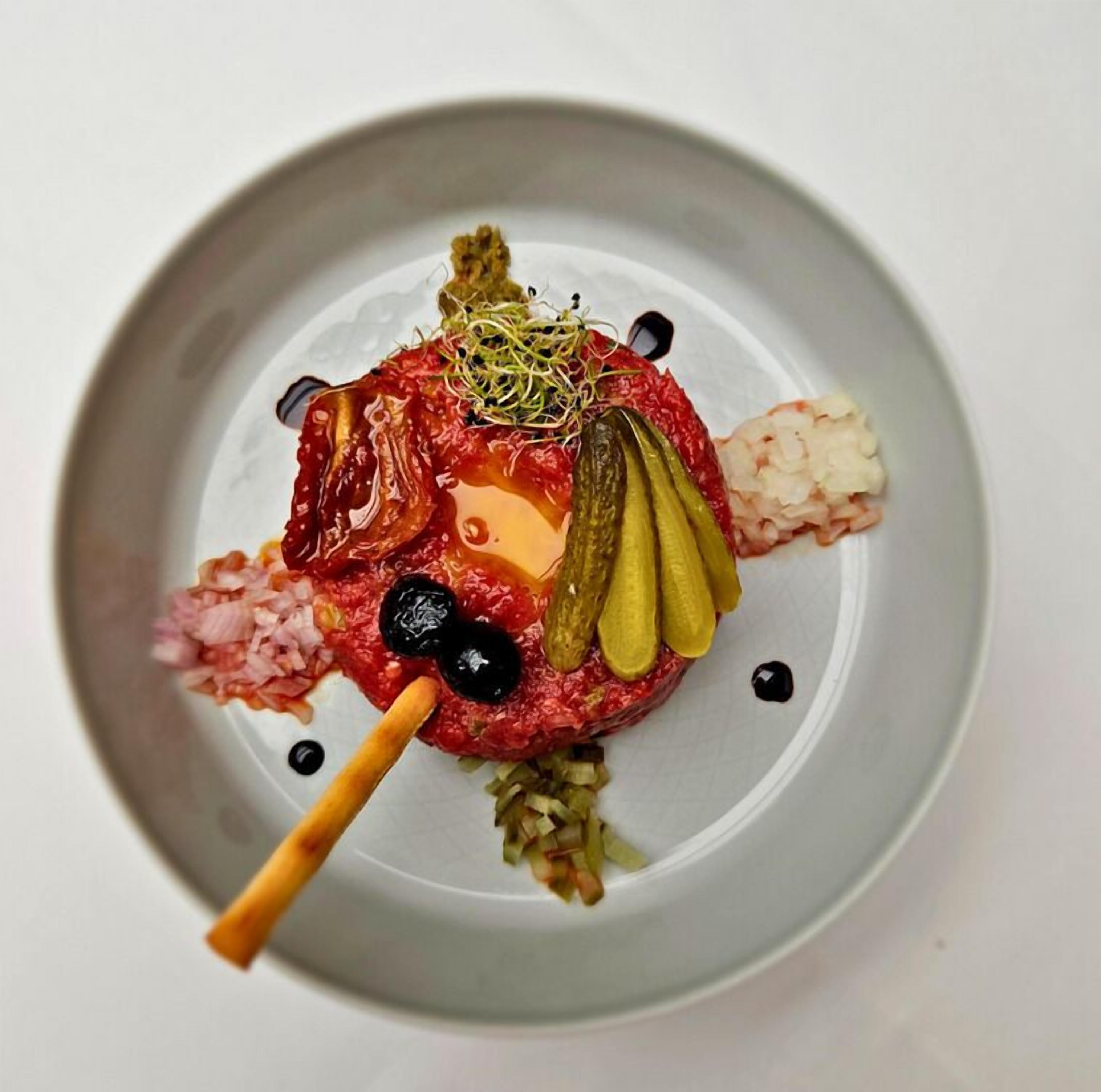 Um prato com um ensopado de molho vermelho, azeitonas, picles e um espeto de madeira.