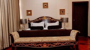 Quarto com uma cama grande, duas luminárias de cabeceira e um banquinho decorativo.