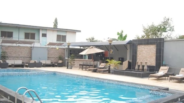 Piscina com espreguiçadeiras e guarda-sóis, cercada por um edifício com fachada de pedra.
