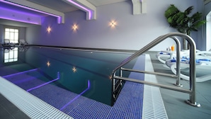 Uma piscina interior com chão de azulejos azuis, um corrimão de metal e luzes fixadas na parede.