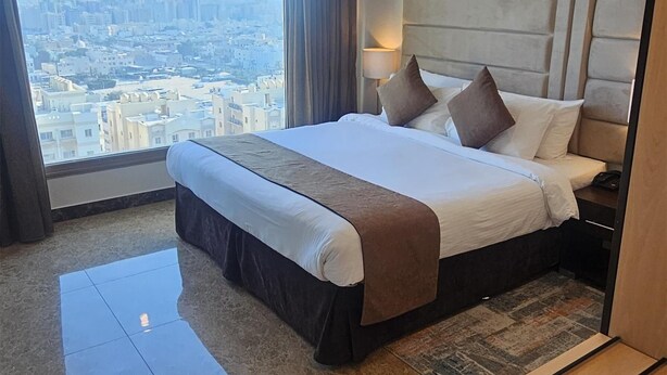 Quarto de hotel com uma cama grande, uma escrivaninha, vista para a cidade e um respiradouro no teto.