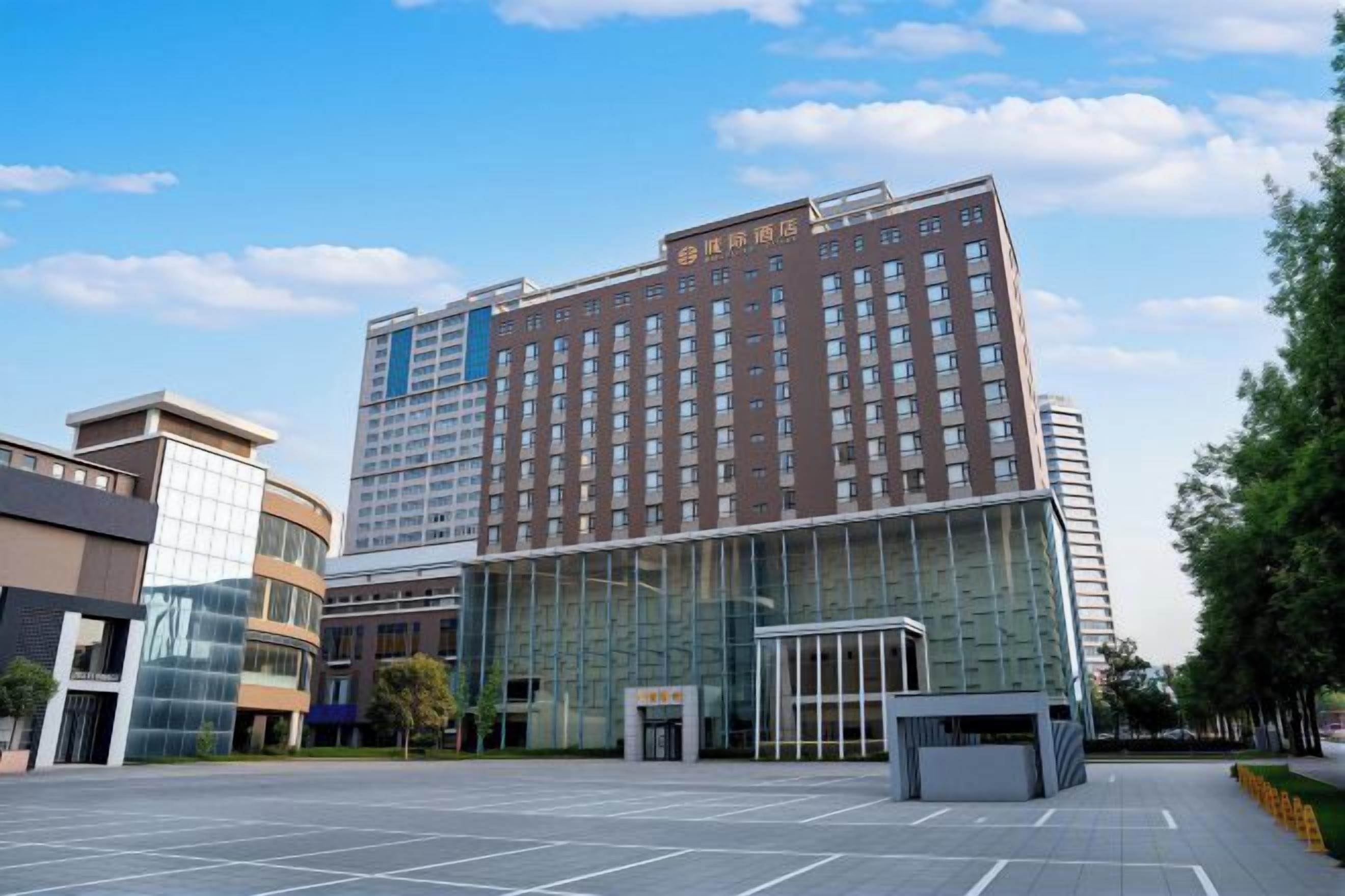 Um hotel moderno com fachada de vidro, entrada central e estacionamento.
