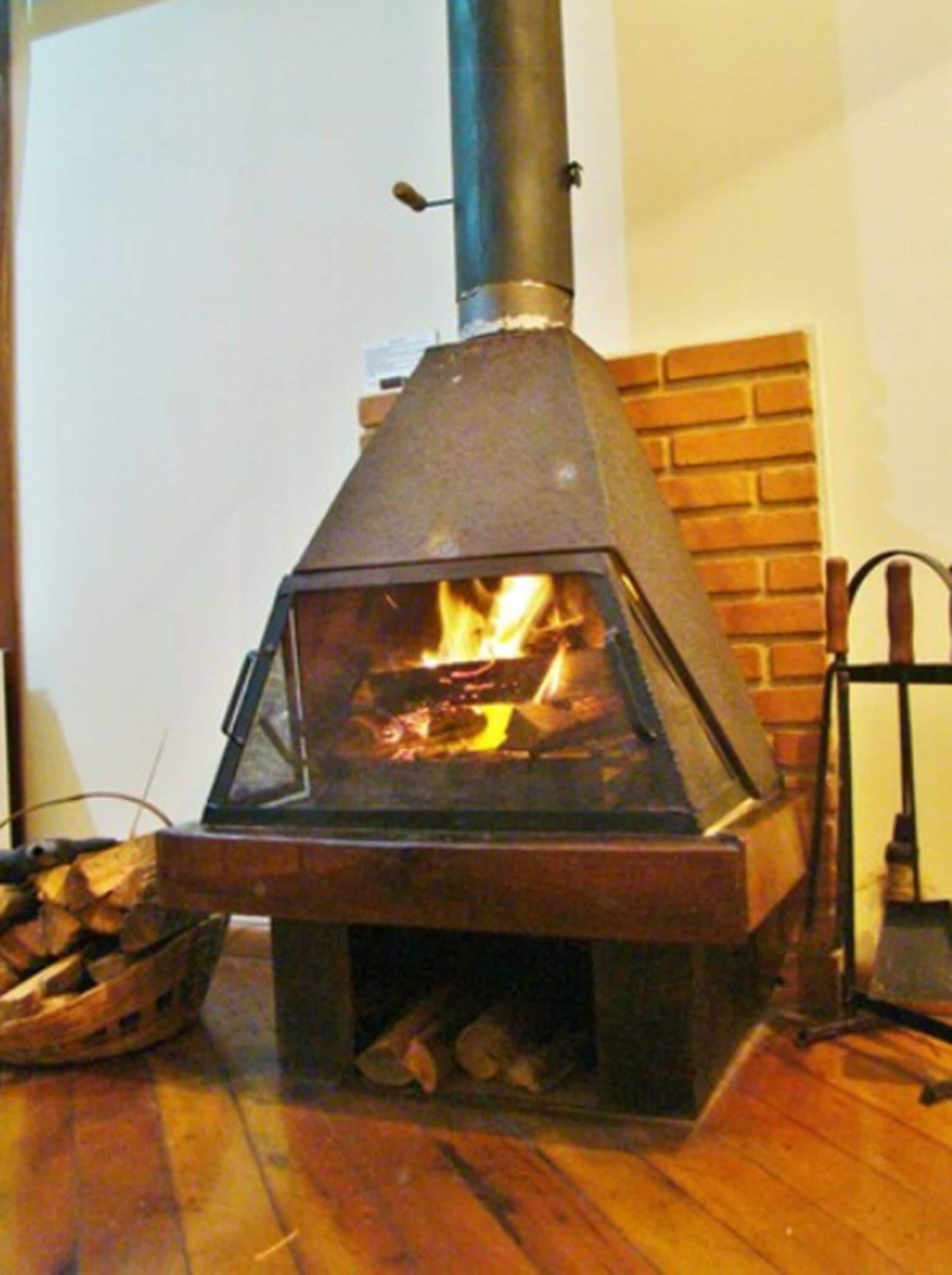 Lareira a lenha com chaminé, lenha no interior e parede de tijolos ao fundo.