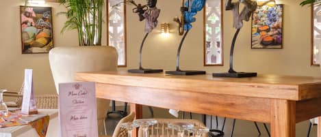 Interior de restaurante com mesa de madeira, cadeiras de vime e um quadro de cardápio.