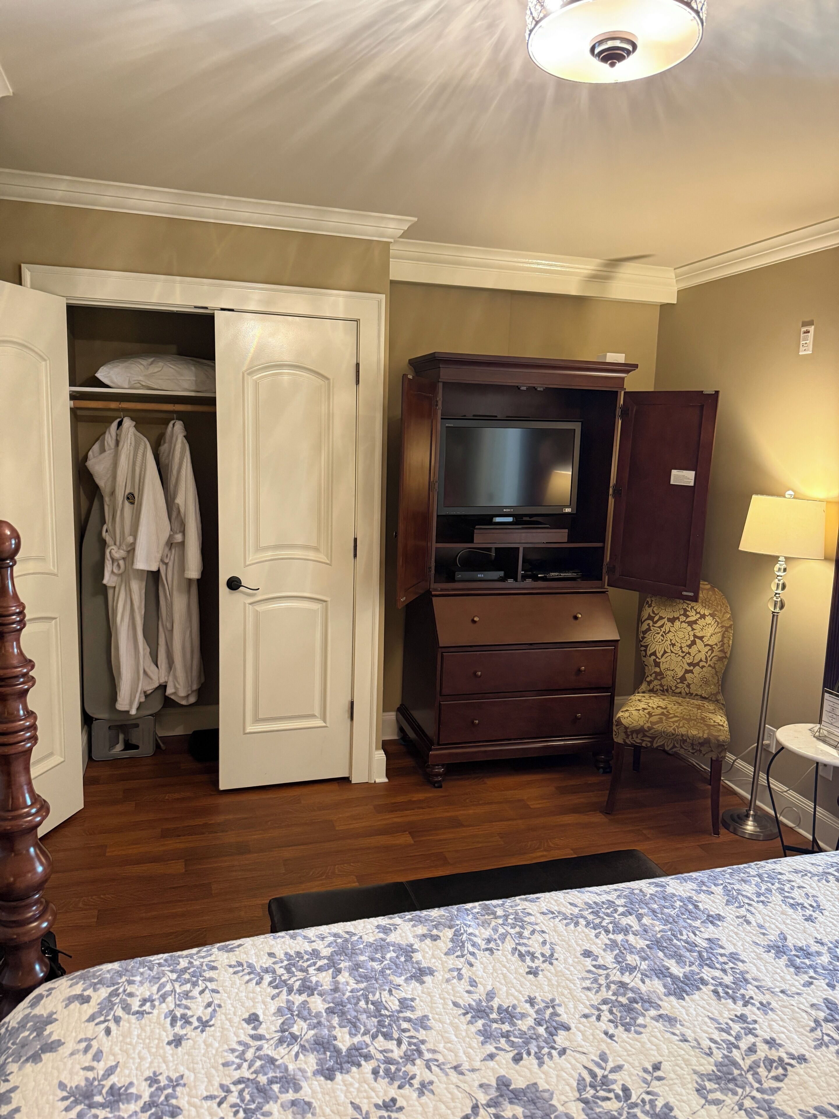 Quarto com cama, guarda-roupa, televisão, uma cadeira e abajur.
