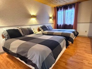 Quarto de hotel com duas camas, piso de madeira e janela com cortinas.