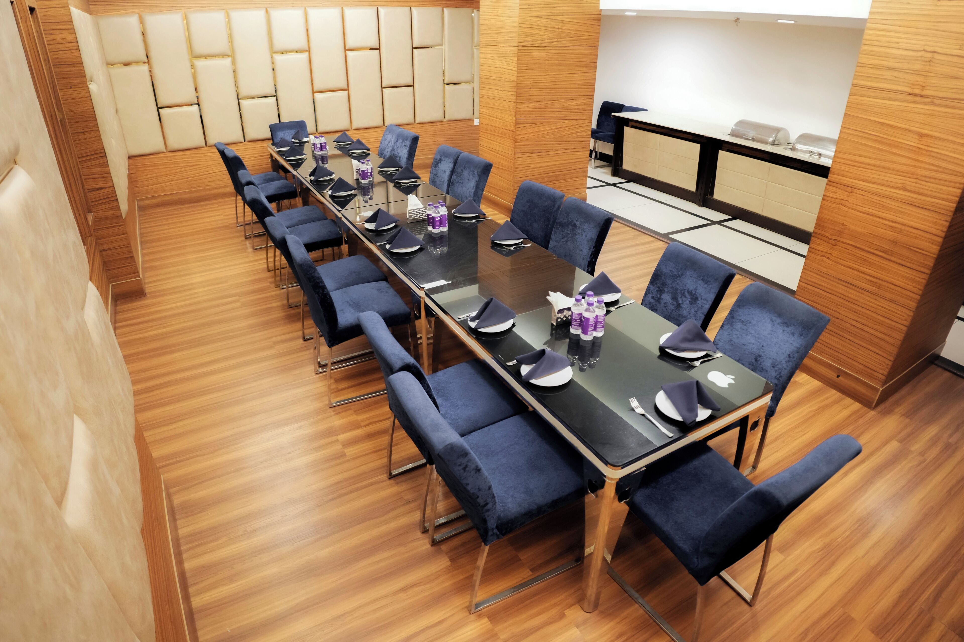 Uma sala de conferências com uma mesa comprida, cadeiras azuis e piso de madeira.