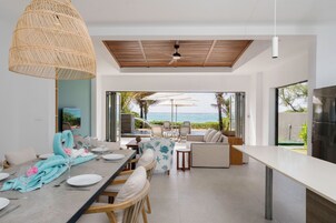 Uma sala de jantar moderna com vista para o mar, um ventilador de teto e uma luminária trançada grande.