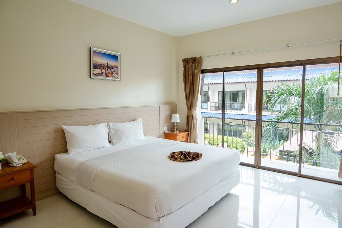 Quarto de hotel com uma cama grande, uma mesa de cabeceira com abajur, telefone e um quadro na parede.