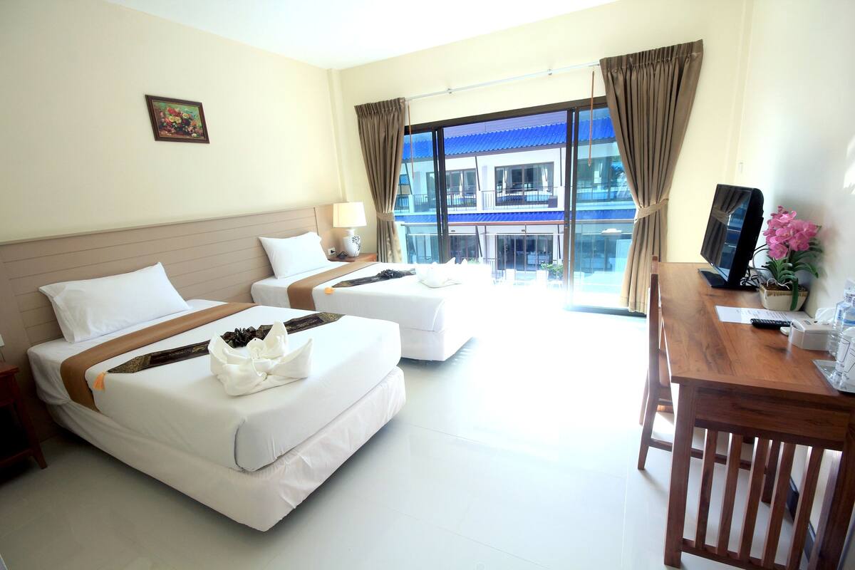 Quarto de hotel com duas camas, uma escrivaninha, televisão e varanda com vista.