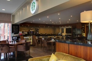 Interior de uma cafeteria Starbucks, com mesas, balcão e painel de cardápio.