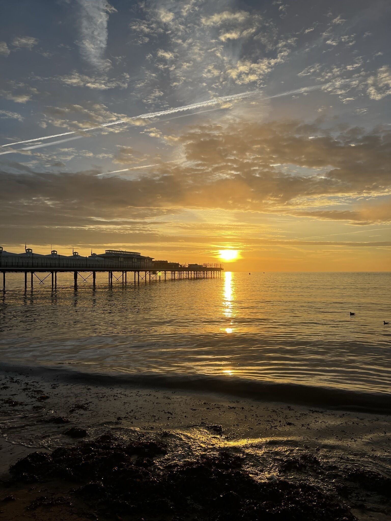 Um pôr do sol sobre um mar tranquilo com um cais que se estende até a água.