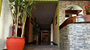 Um saguão de hotel com uma grande planta em vaso, piso de azulejos e um balcão de recepção.
