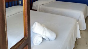 Quarto com duas camas, cabeceira de madeira, toalha branca e parede azul.