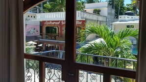 Quarto com uma janela ampla que dá para um restaurante e área externa com mesas.