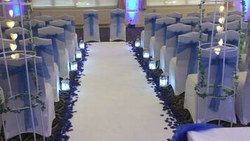 Um corredor de casamento com cadeiras brancas e fitas azuis, iluminado por lanternas e decorado com flores.