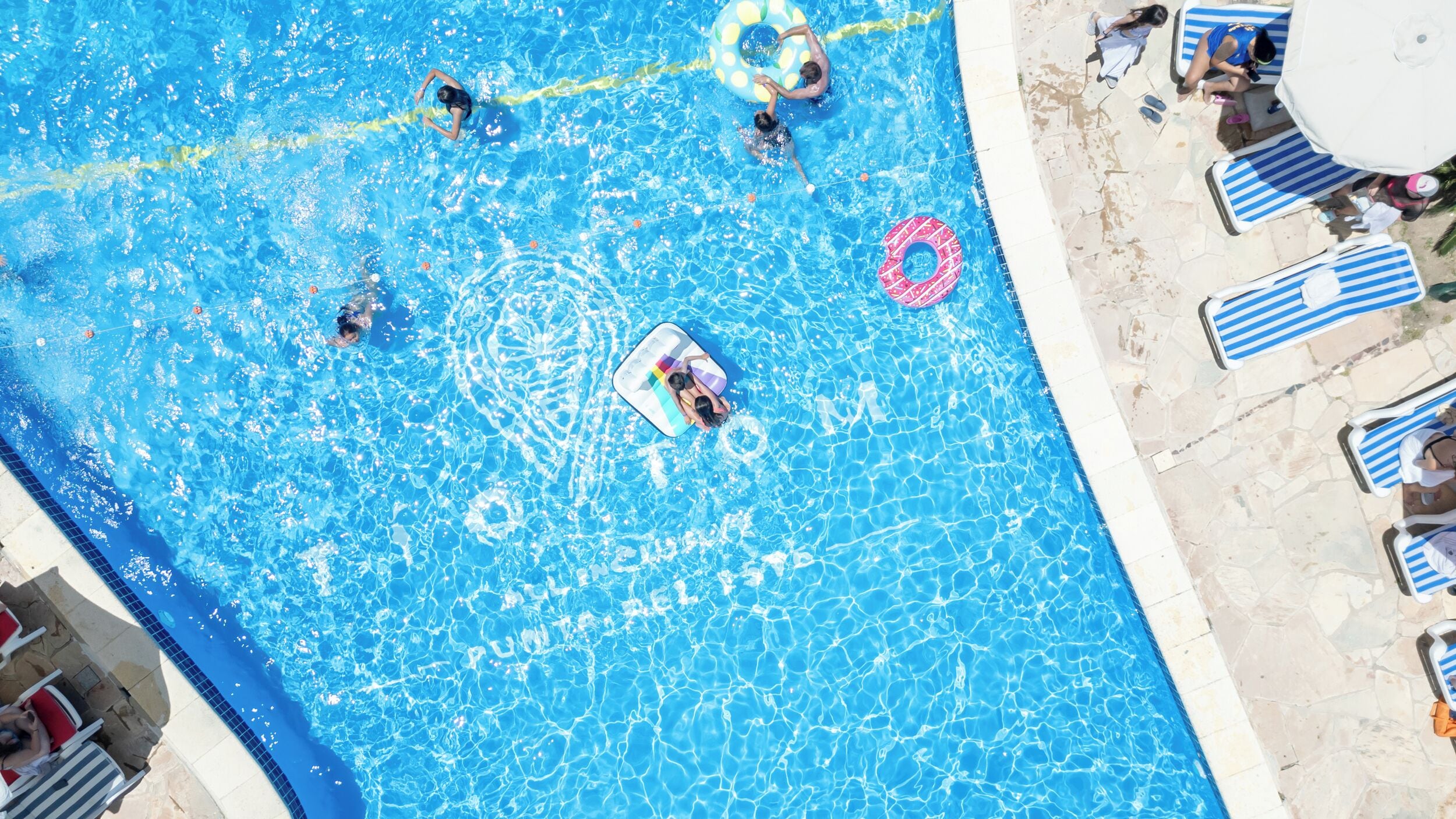 Vista aérea de uma piscina com várias pistas, espreguiçadeiras e área com guarda-sóis.