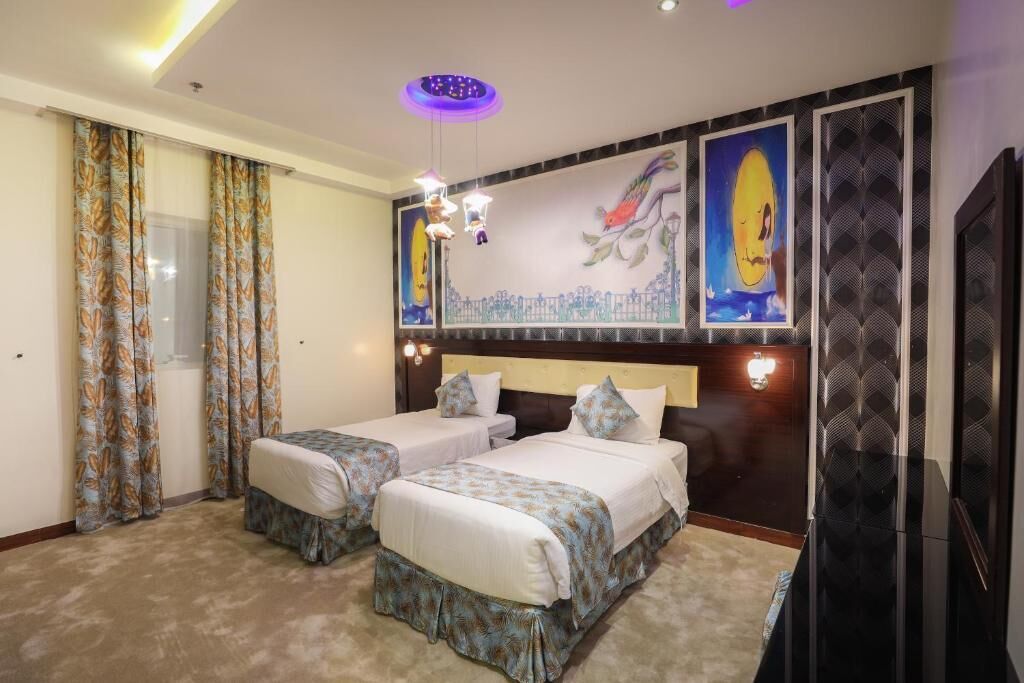 Quarto de hotel com duas camas, um mural grande, uma TV de tela plana e um lustre.