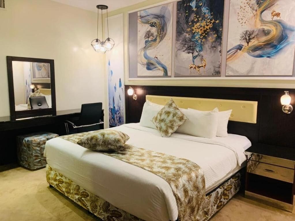Quarto de hotel com cama, escrivaninha, cadeira, espelho e obras de arte na parede.