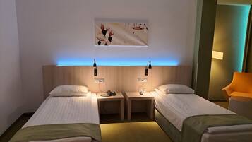 Quarto de hotel com duas camas de solteiro, mesa de cabeceira com telefone e controle remoto, obra de arte na parede e abajur.