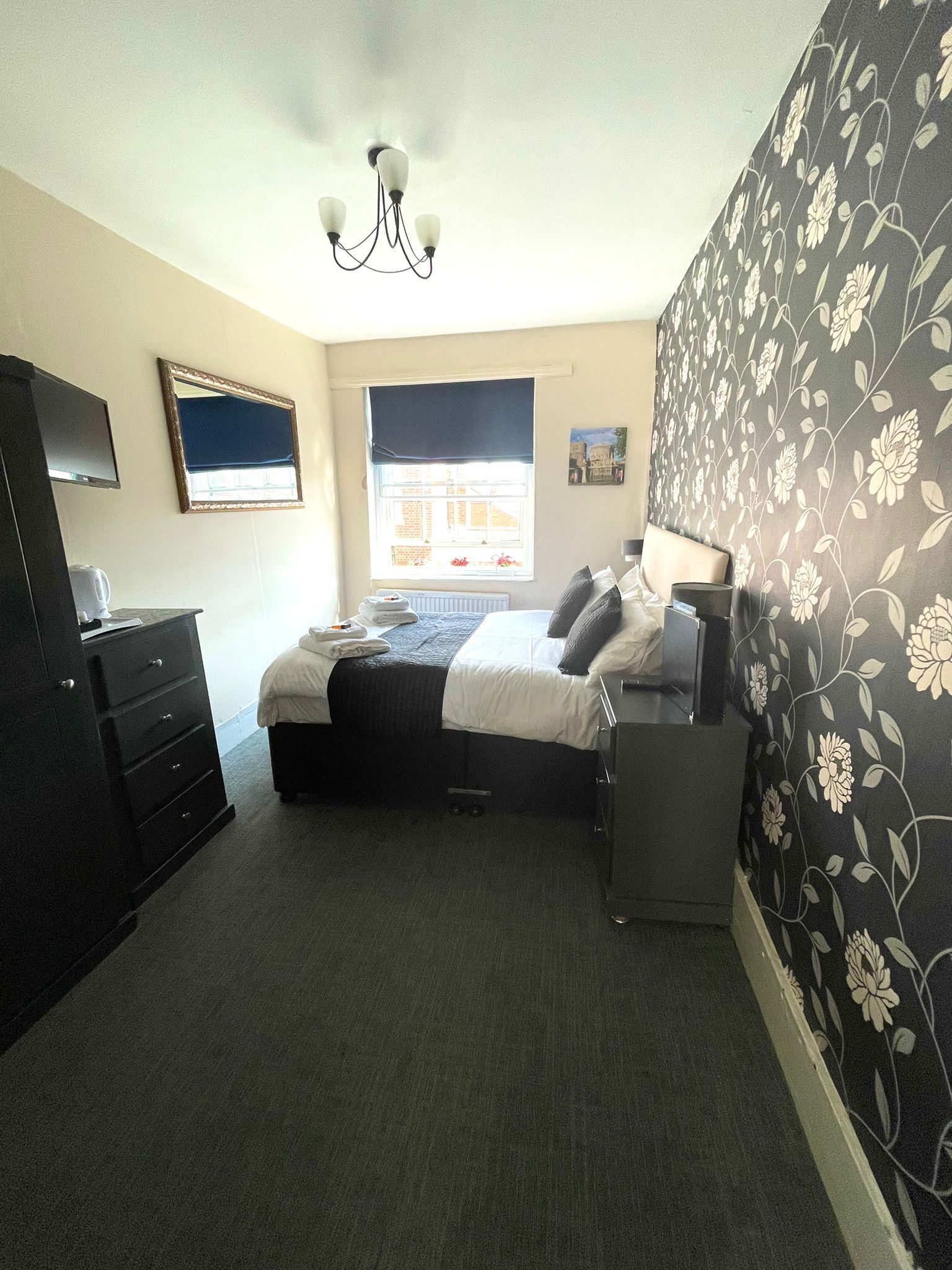 Quarto com cama, cômoda, televisão, janela e papel de parede floral.