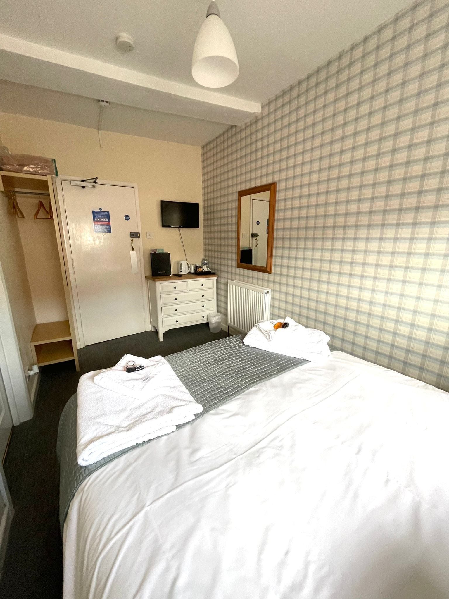 Quarto de hotel com uma cama, penteadeira, espelho, televisão e radiador.