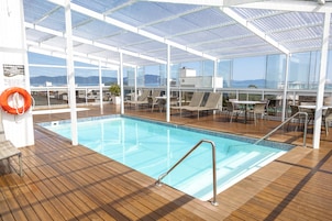 Uma área de piscina ensolarada com vista clara para o mar e montanhas ao fundo.