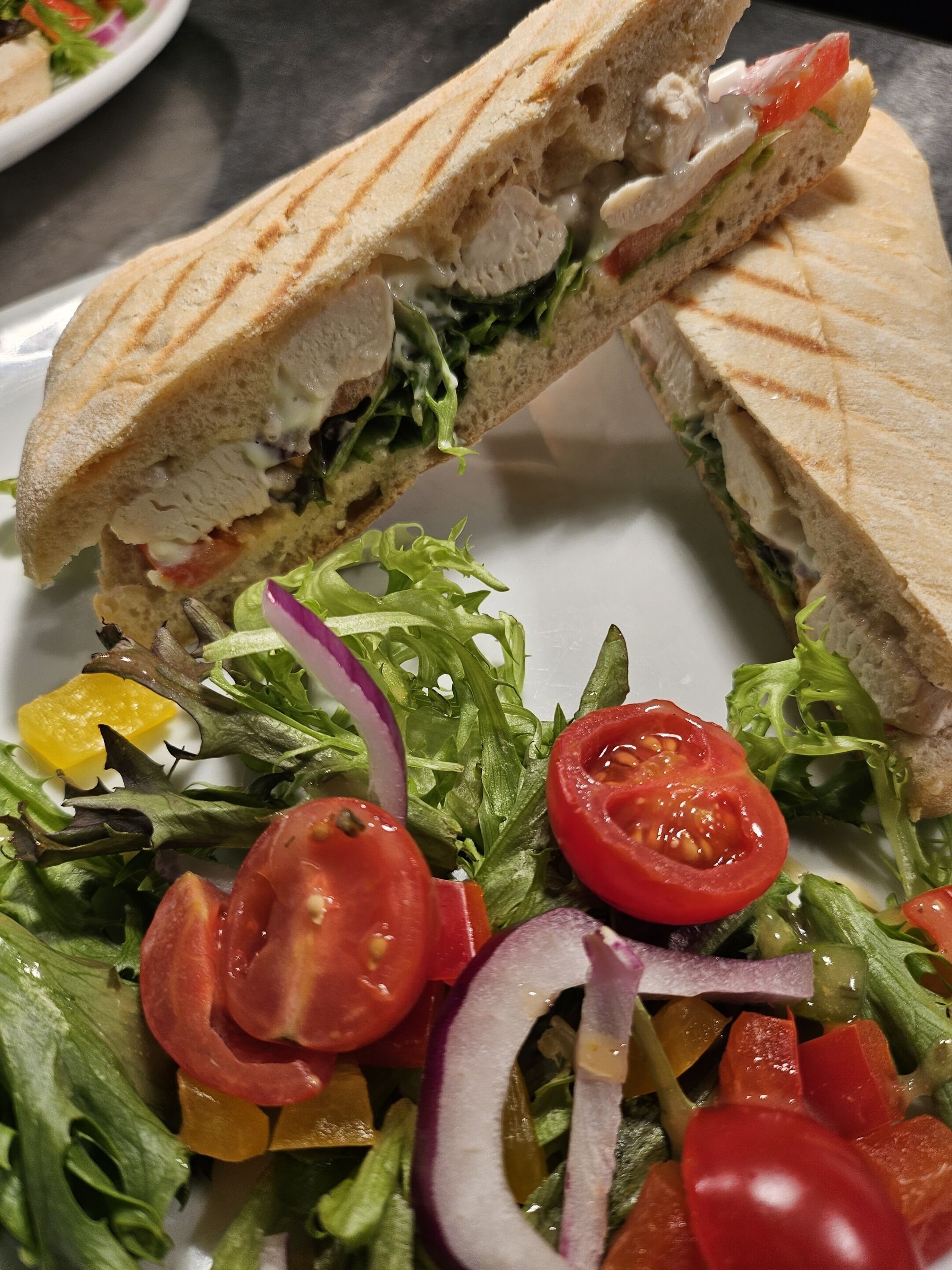 Um sanduíche cortado ao meio, servido em um prato com uma salada.