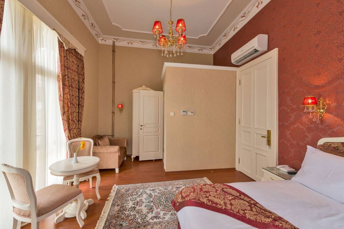 Quarto de hotel com cama, poltrona, mesinha, guarda-roupa, lustre e luminária de parede.