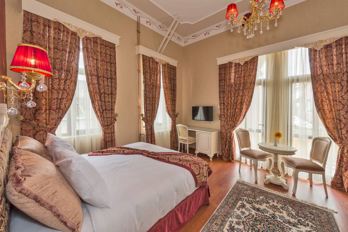 Quarto de hotel com uma cama grande, escrivaninha, televisão e pequena área de refeições com cadeiras e mesa.