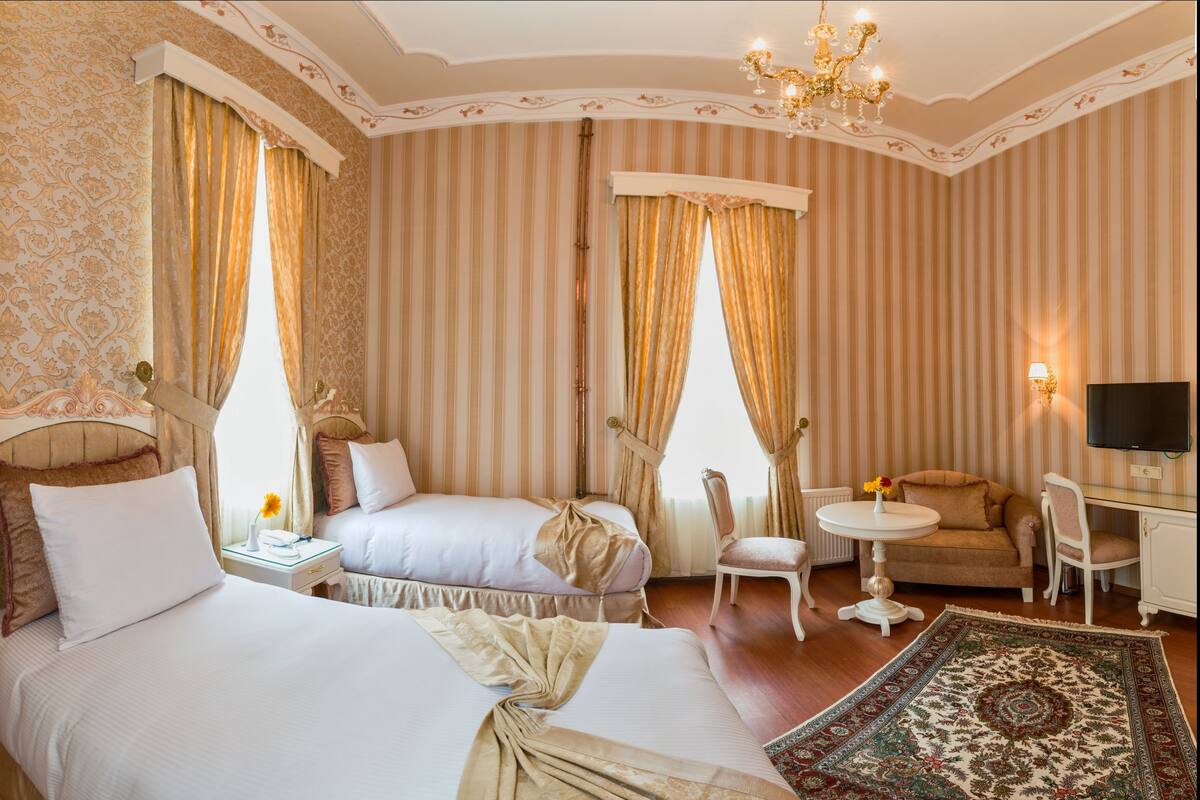 Quarto de hotel com duas camas, área de estar com sofá e poltronas, uma mesinha e televisão.