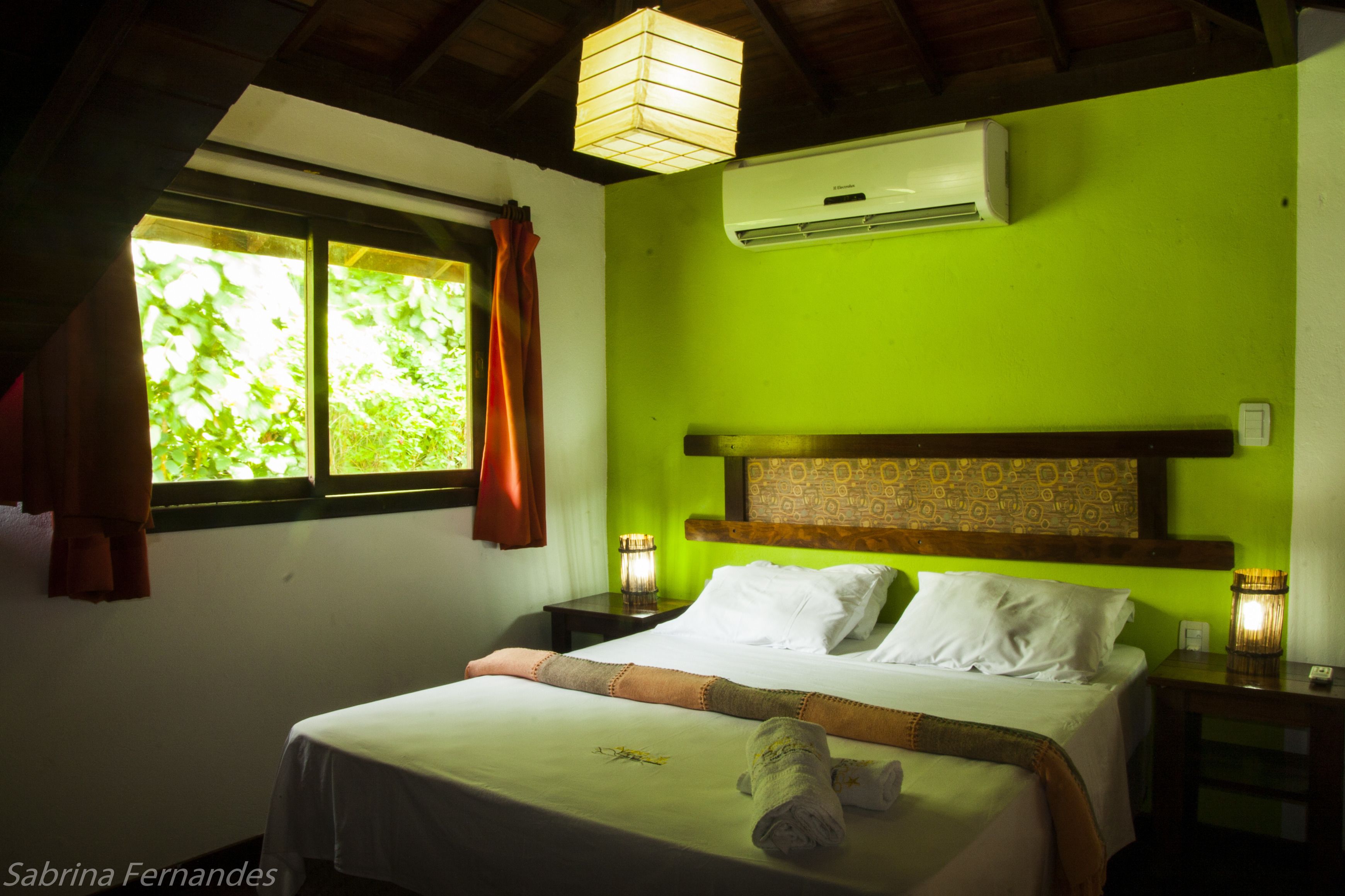 Quarto de hotel com uma cama, janela com cortinas, ar condicionado e abajures.