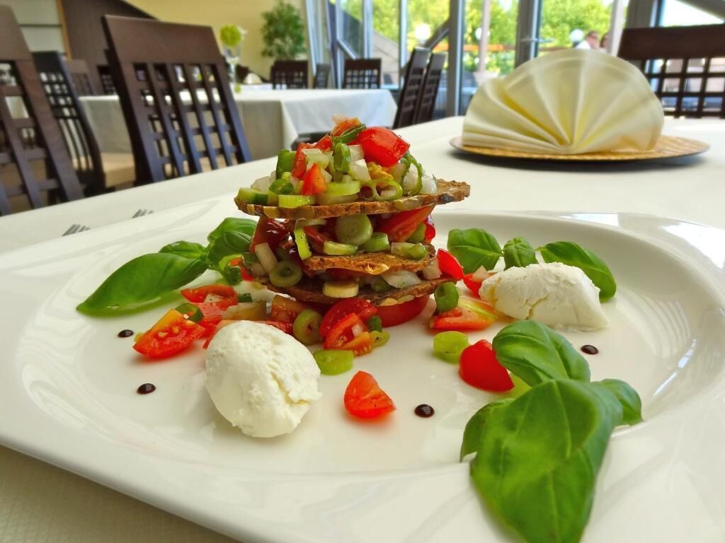 Prato branco com salada em camadas, bolinhas de mussarela e folhas de manjericão.