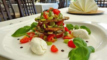 Prato branco com salada em camadas, bolinhas de mussarela e folhas de manjericão.