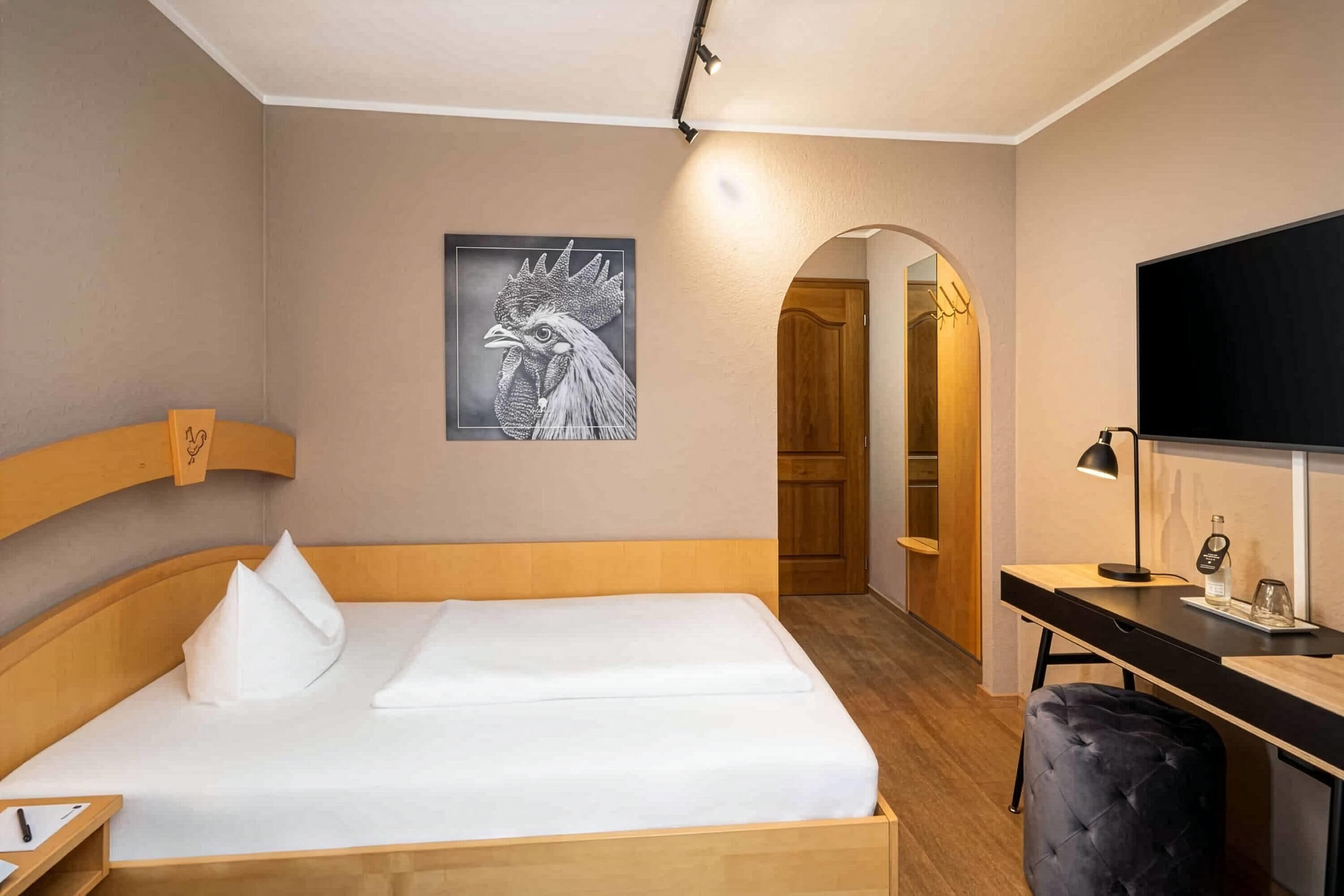 Quarto de hotel com cama, escrivaninha, cadeira, televisão e quadro na parede.