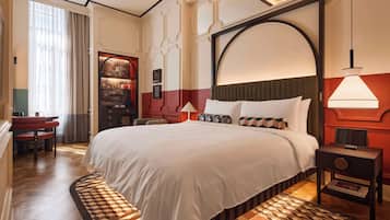 Quarto de hotel com uma cama grande, uma escrivaninha, uma cadeira, uma televisão e uma estante de livros.